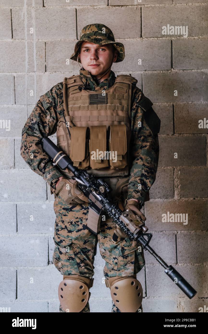 A soldier in uniform stands in front of a stone wall in full war gear ...