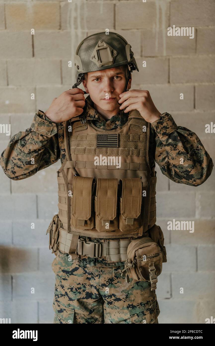A soldier in uniform stands in front of a stone wall in full war gear ...