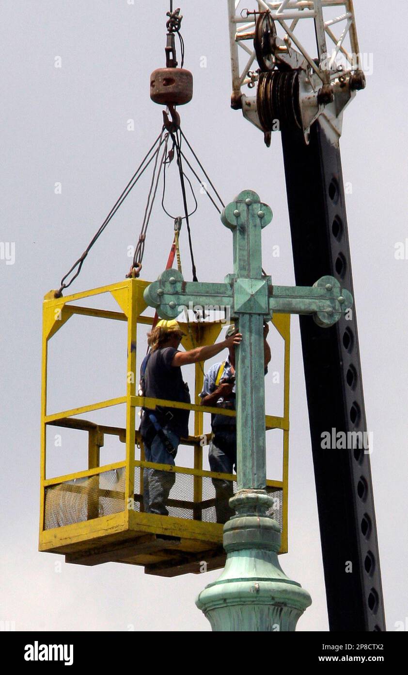 Workers position a cross atop the steeple of Holy Family Catholic ...