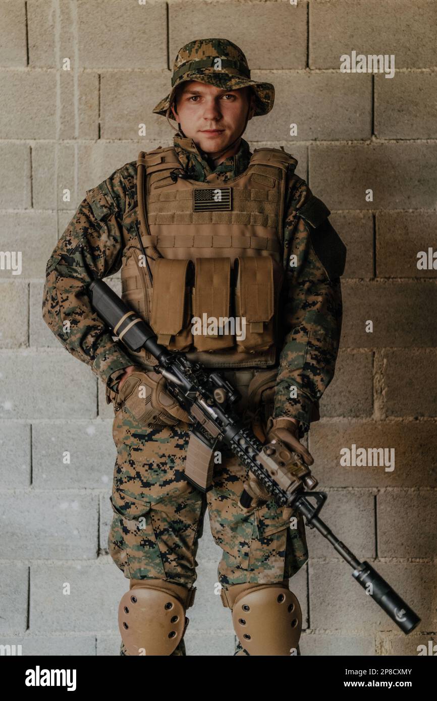A soldier in uniform stands in front of a stone wall in full war gear ...