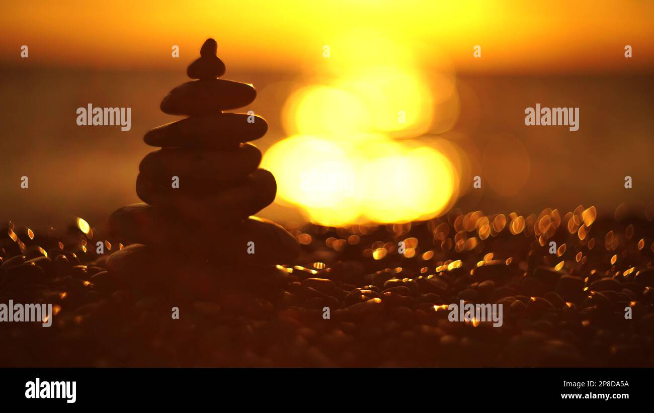 Balanced rock pyramid on pebbles beach. Golden sea bokeh on background ...
