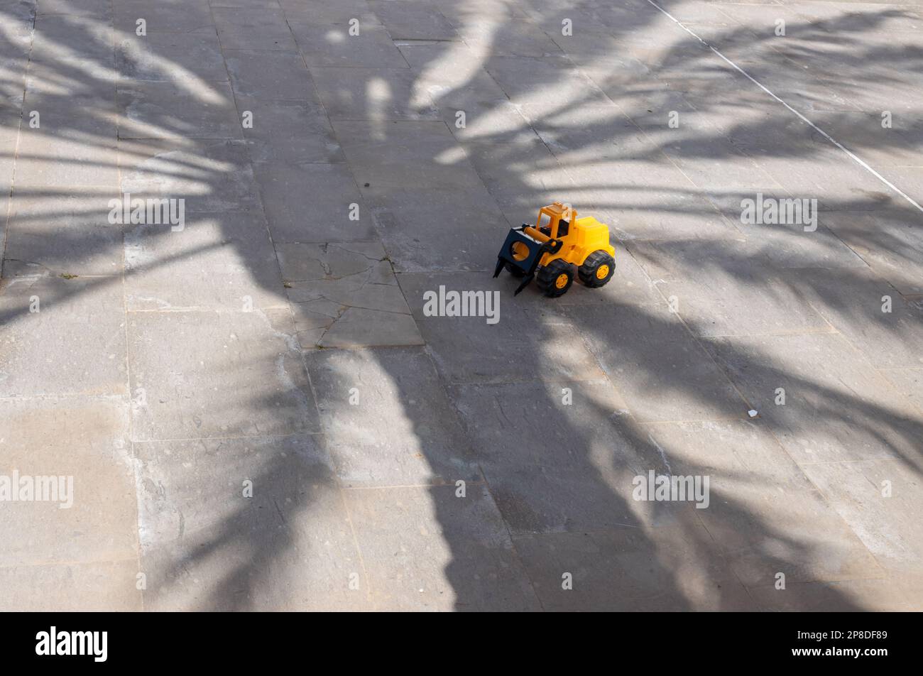 Street with stone tiles. Forgotten yellow children toy - tractor in a ...