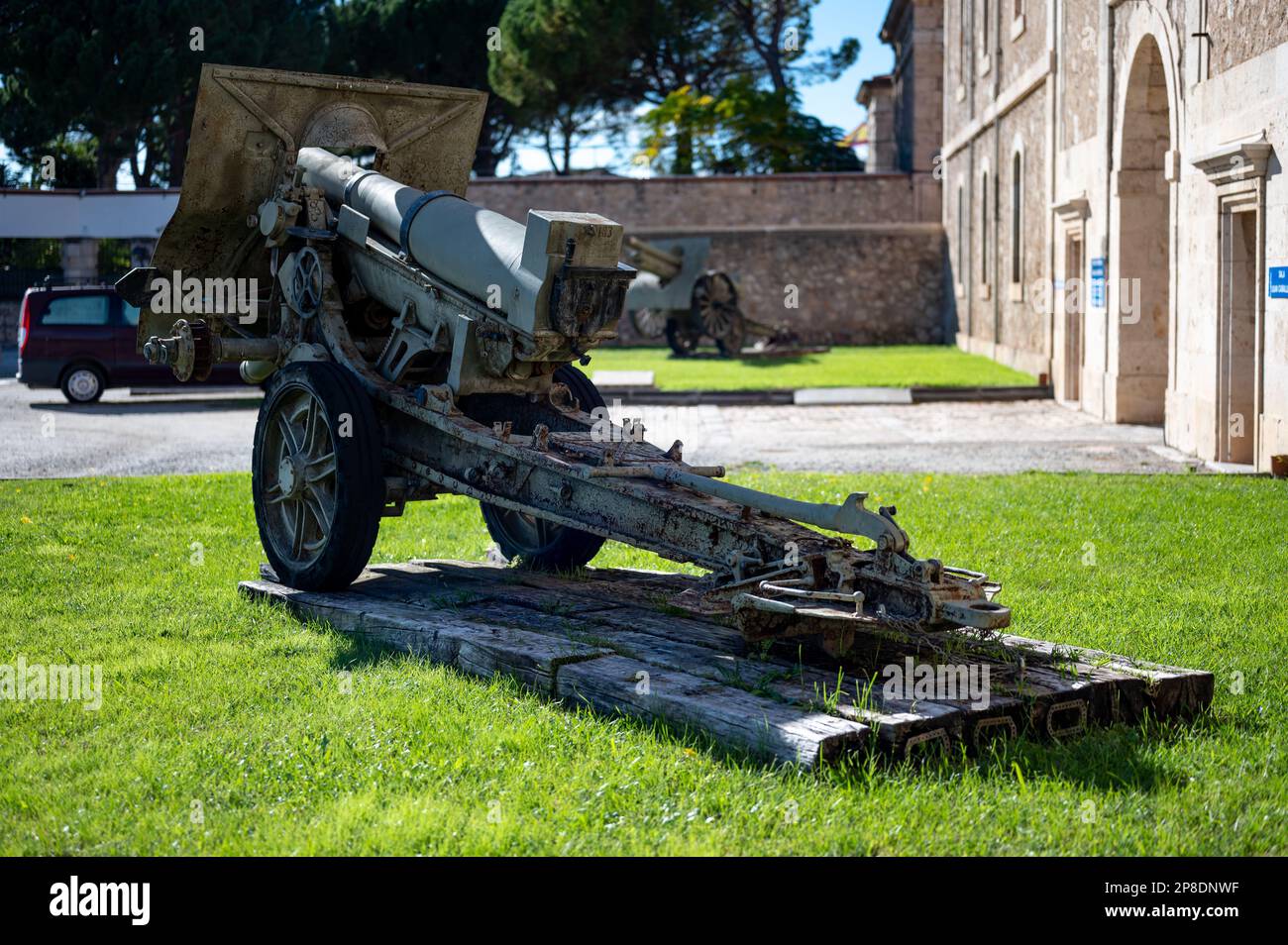 A vintage cannon standing in a grassy field with several cars parked in ...