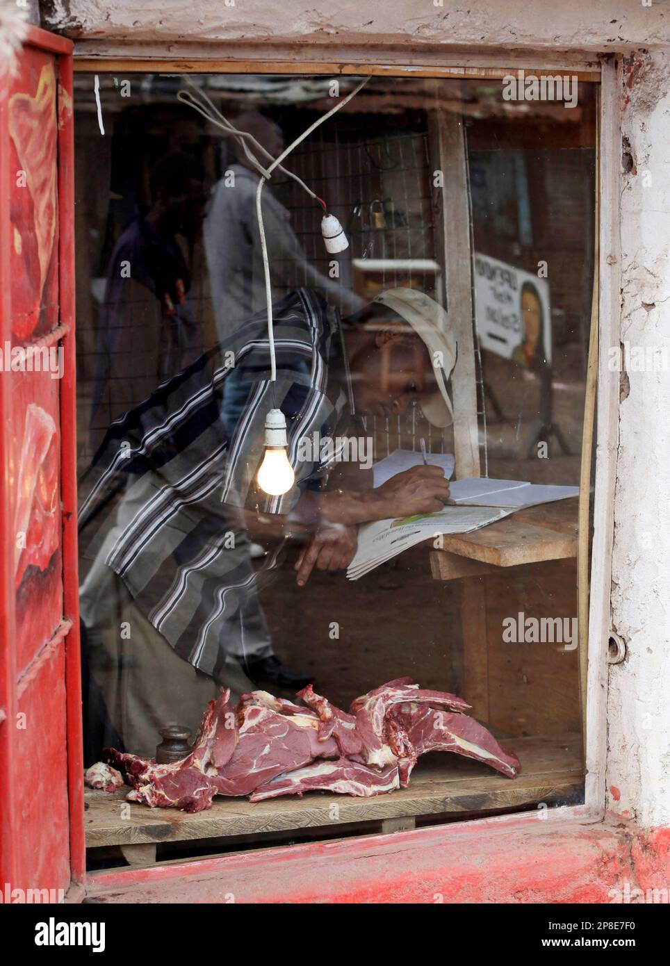 A butcher works in his shop, with un refrigerated meat in the window ...