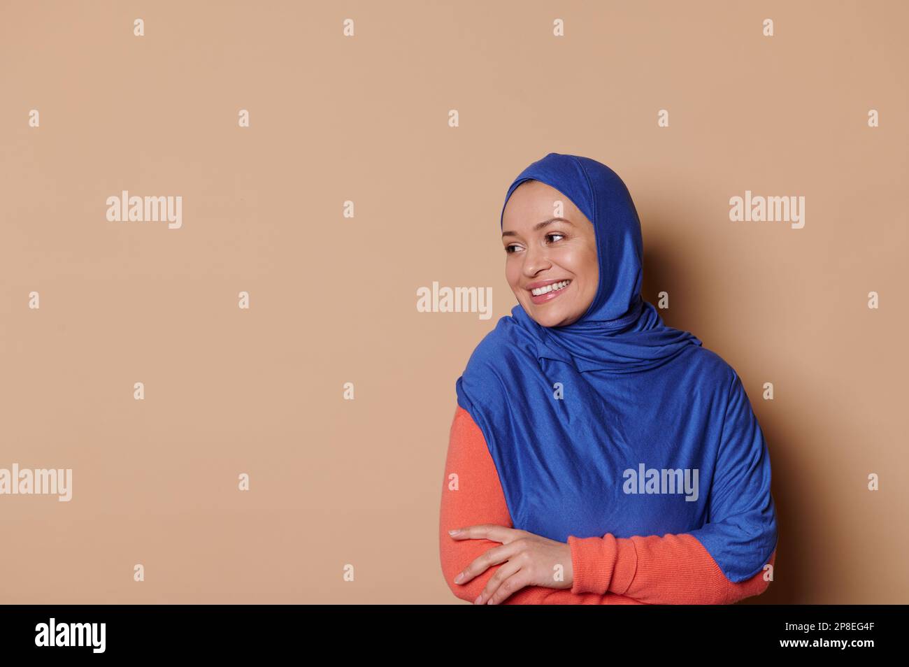 Arab Muslim woman in blue hijab, smiling looking aside at ad space on ...