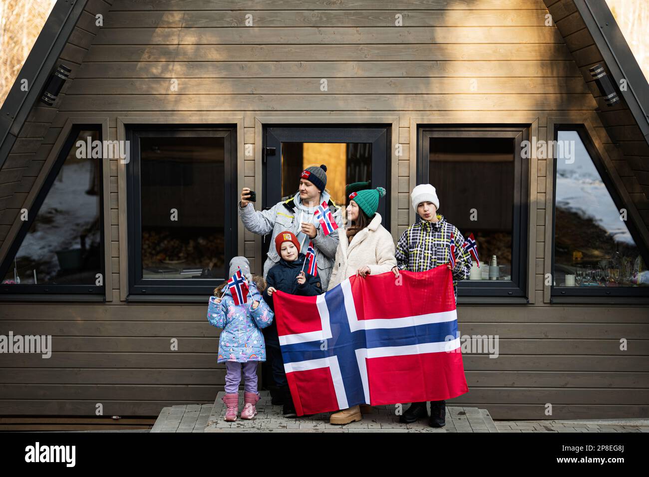 Portrait of family with kids outside cabin house holding Norway flags ...