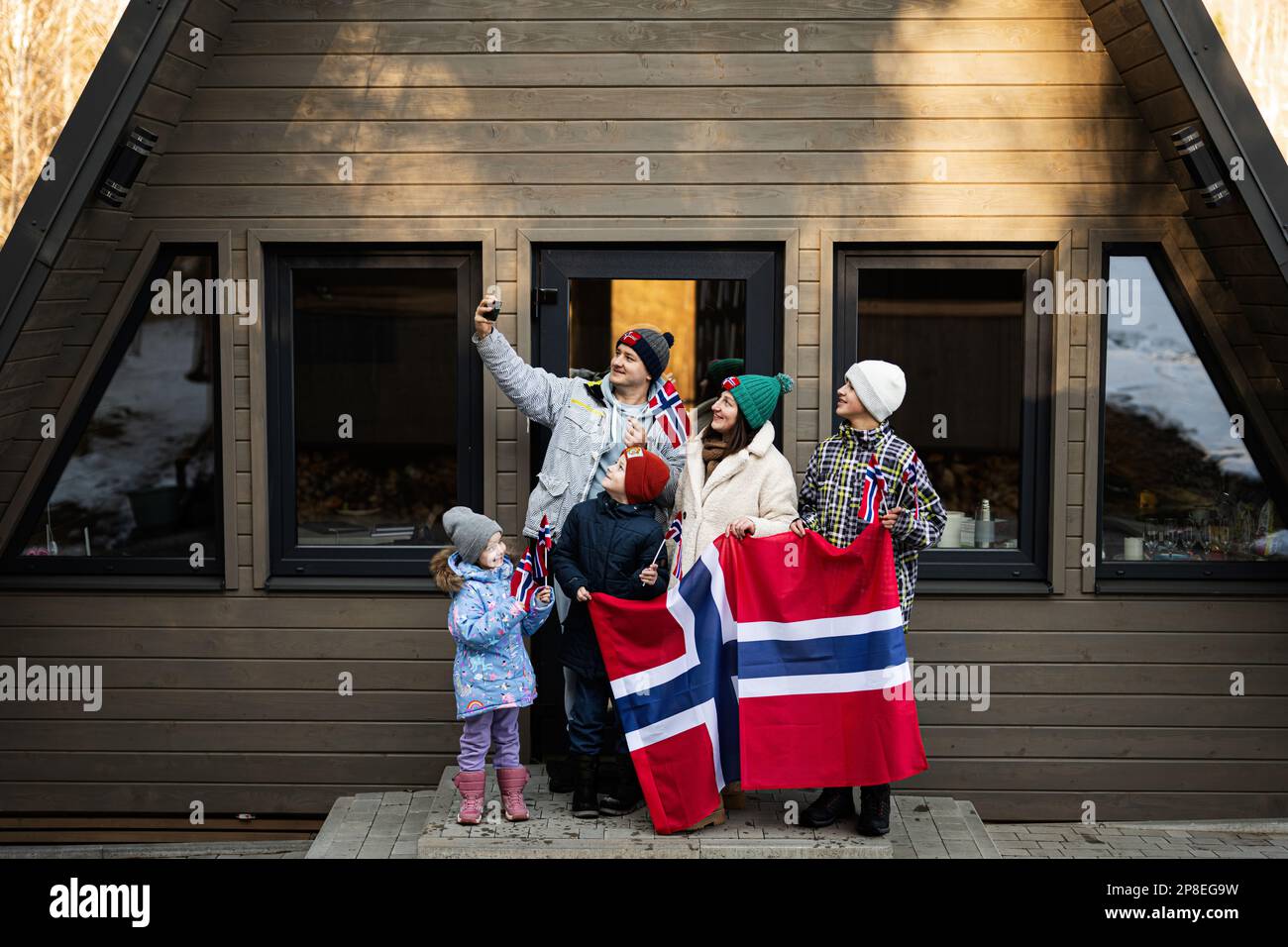 Portrait of family with kids outside cabin house holding Norway flags ...