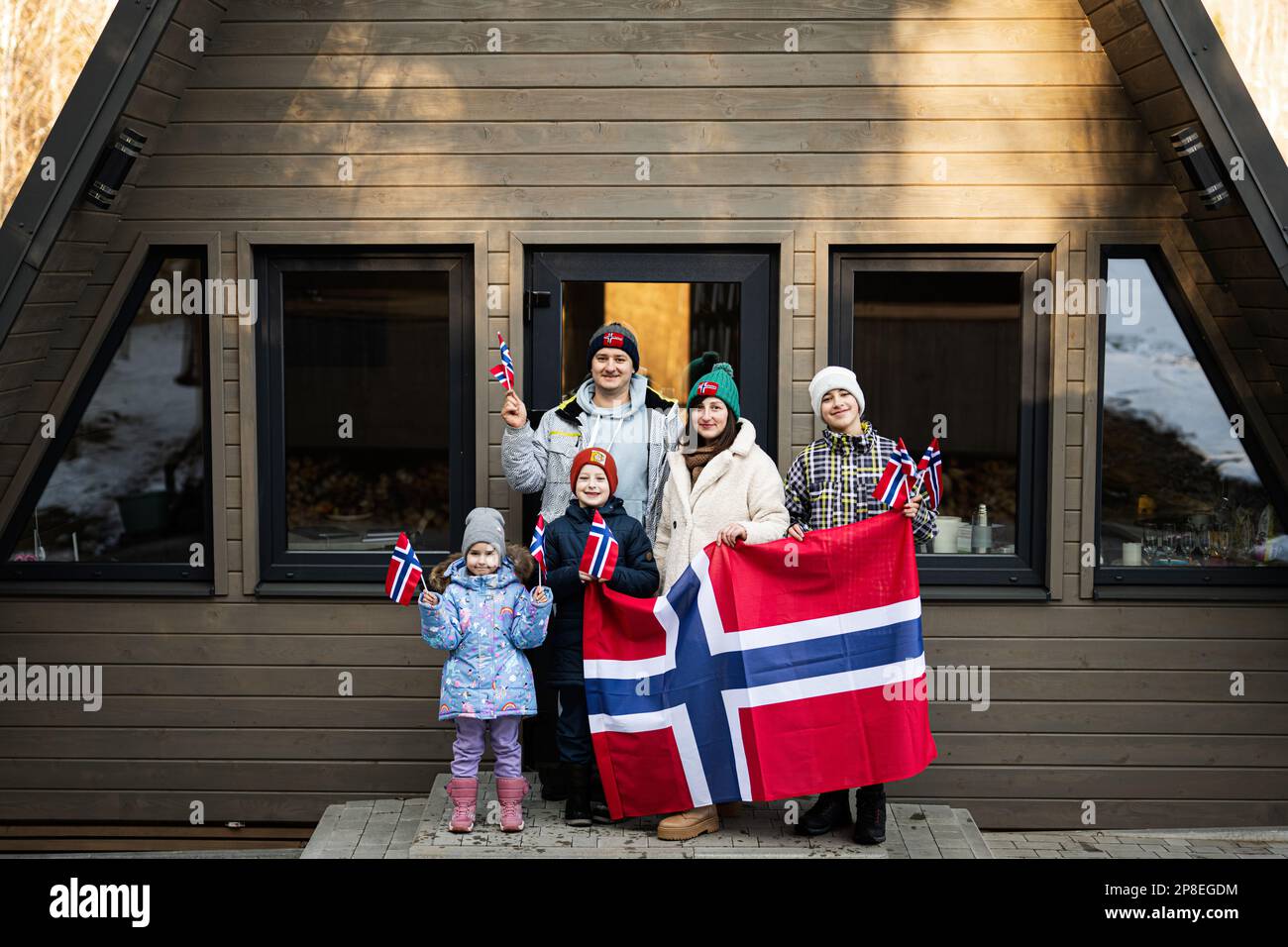 Portrait of family with kids outside cabin house holding Norway flags ...