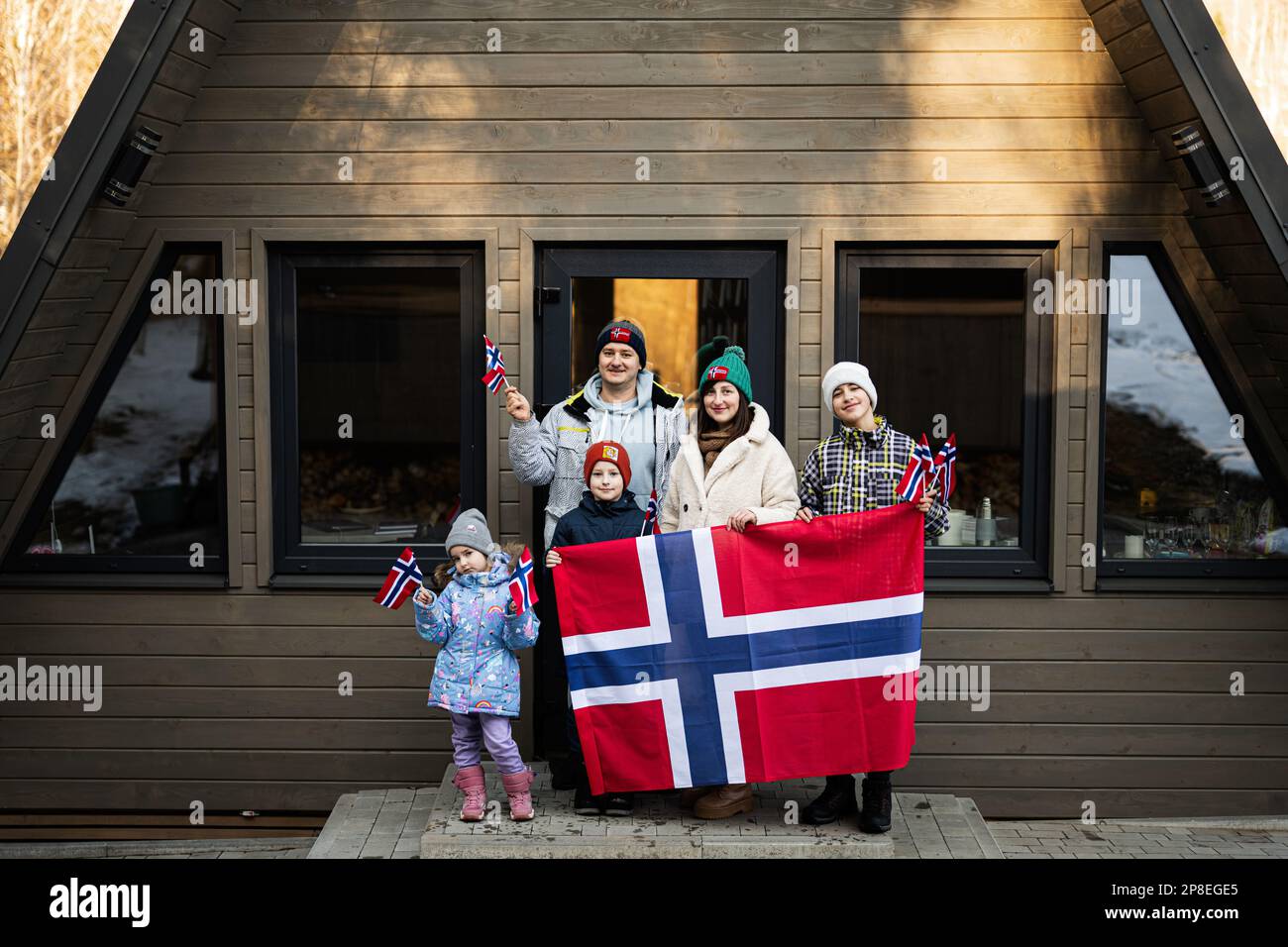 Portrait of family with kids outside cabin house holding Norway flags ...
