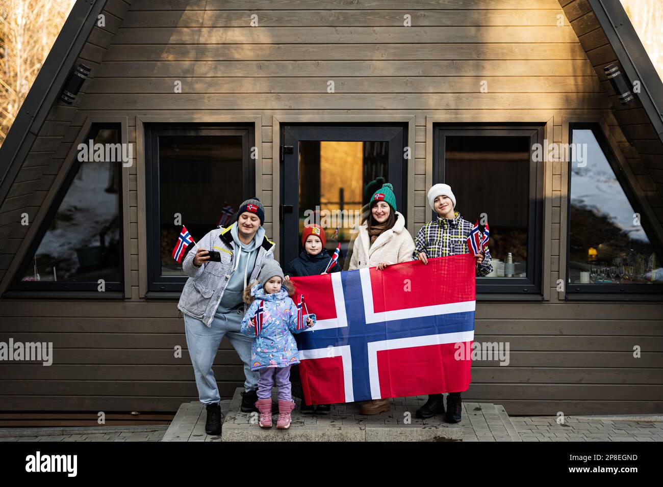 Portrait of family with kids outside cabin house holding Norway flags ...