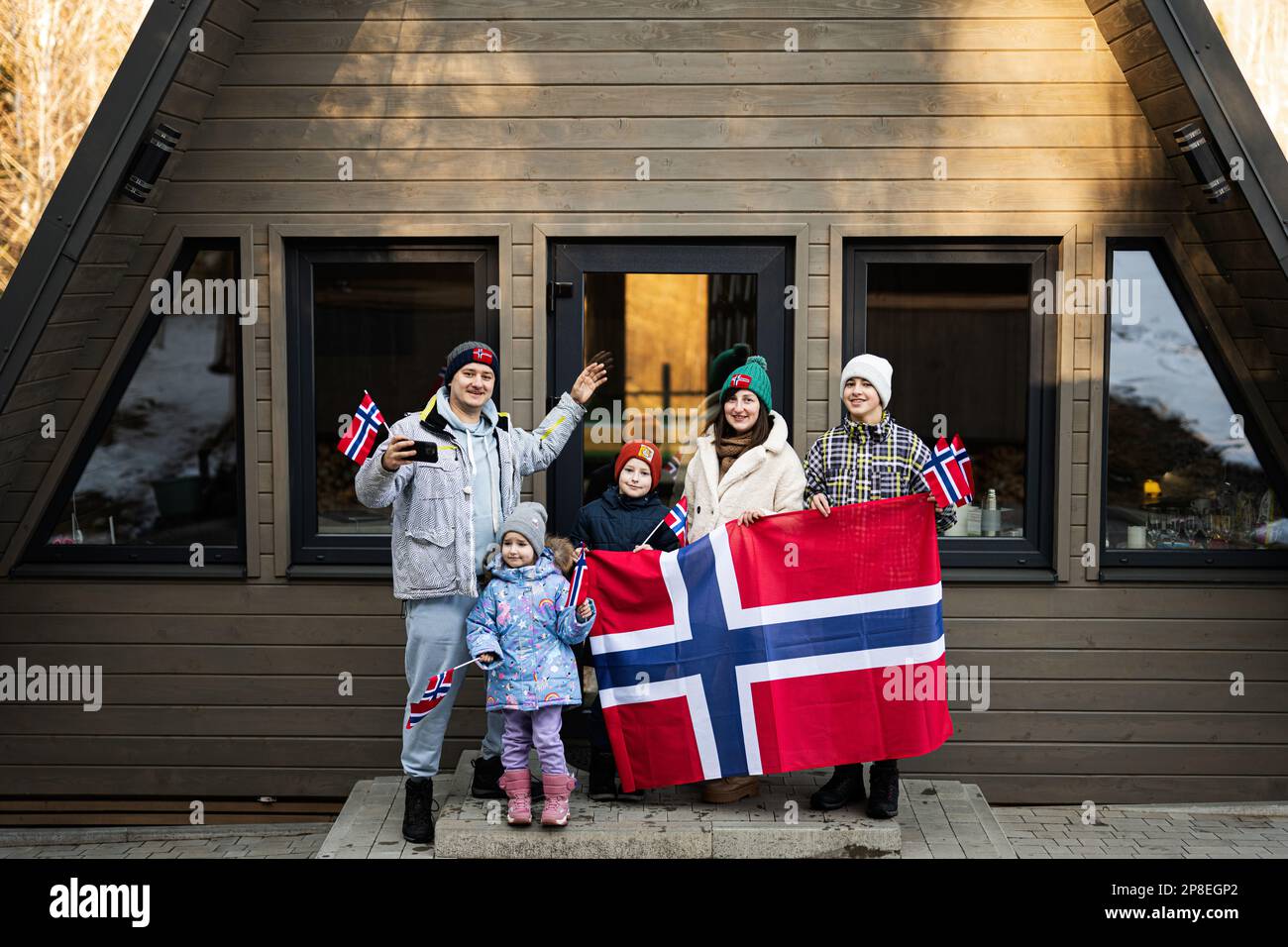 Portrait of family with kids outside cabin house holding Norway flags ...