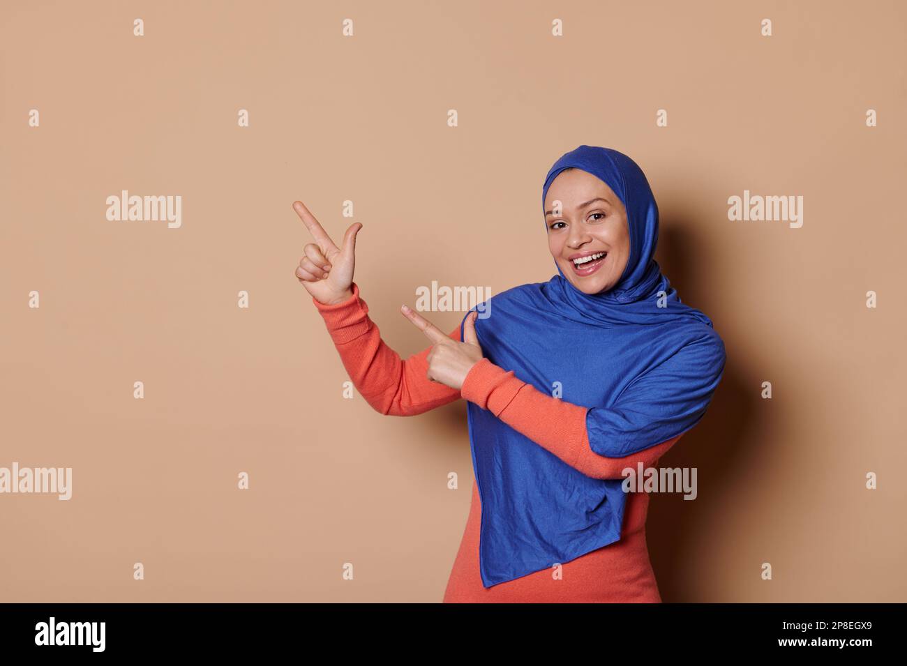 Cheerful Arab Muslim woman with head covered in blue hijab, pointing at ...