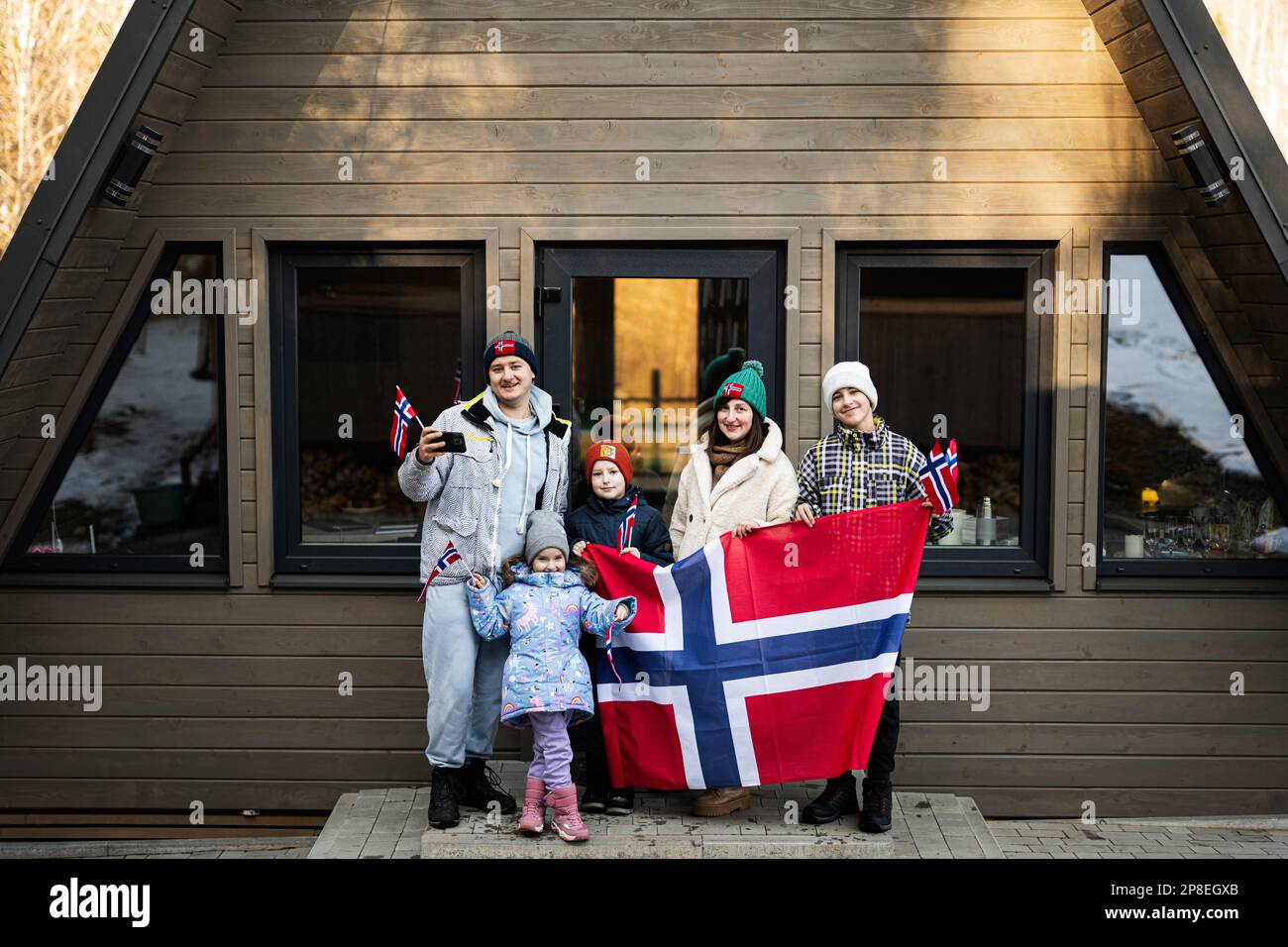 Portrait of family with kids outside cabin house holding Norway flags ...