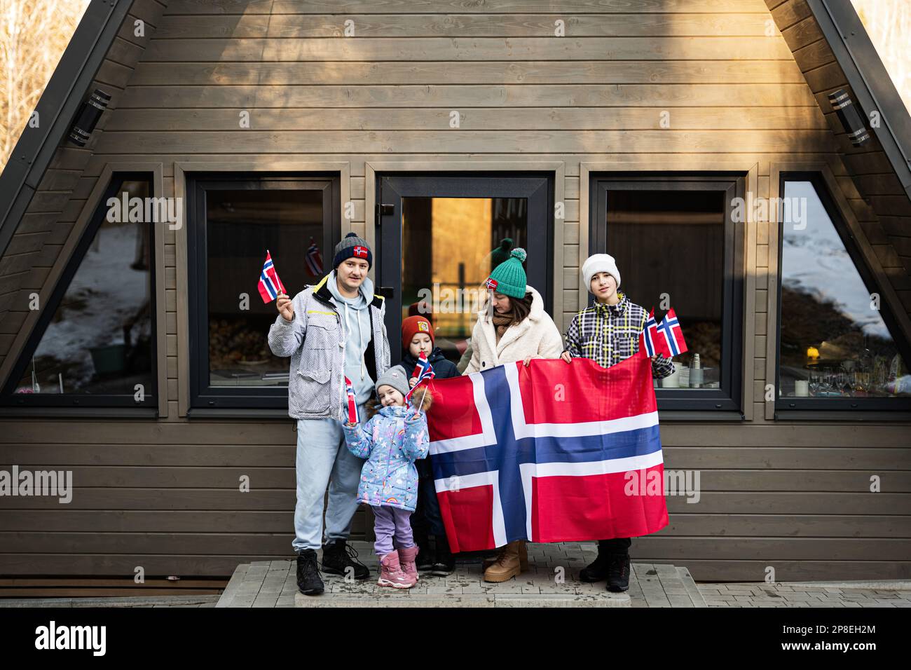 Portrait of family with kids outside cabin house holding Norway flags ...