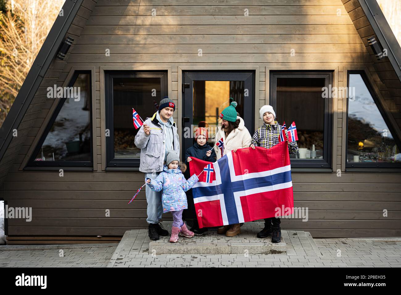 Portrait of family with kids outside cabin house holding Norway flags ...