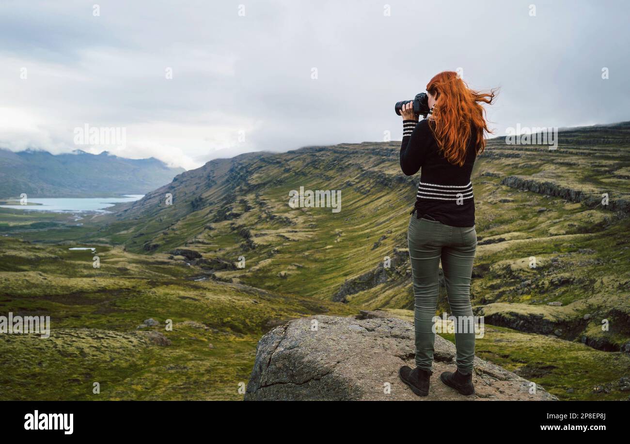 Rear view of a woman taking a photograph of a distant lake in rural ...