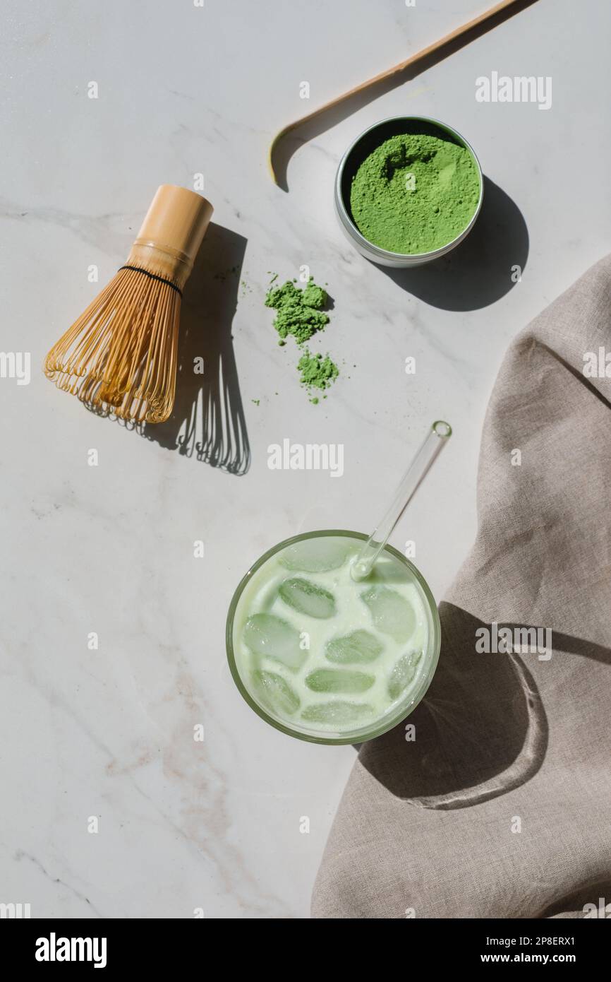 Overhead view of a glass of iced matcha drink, bamboo whisk, matcha ...