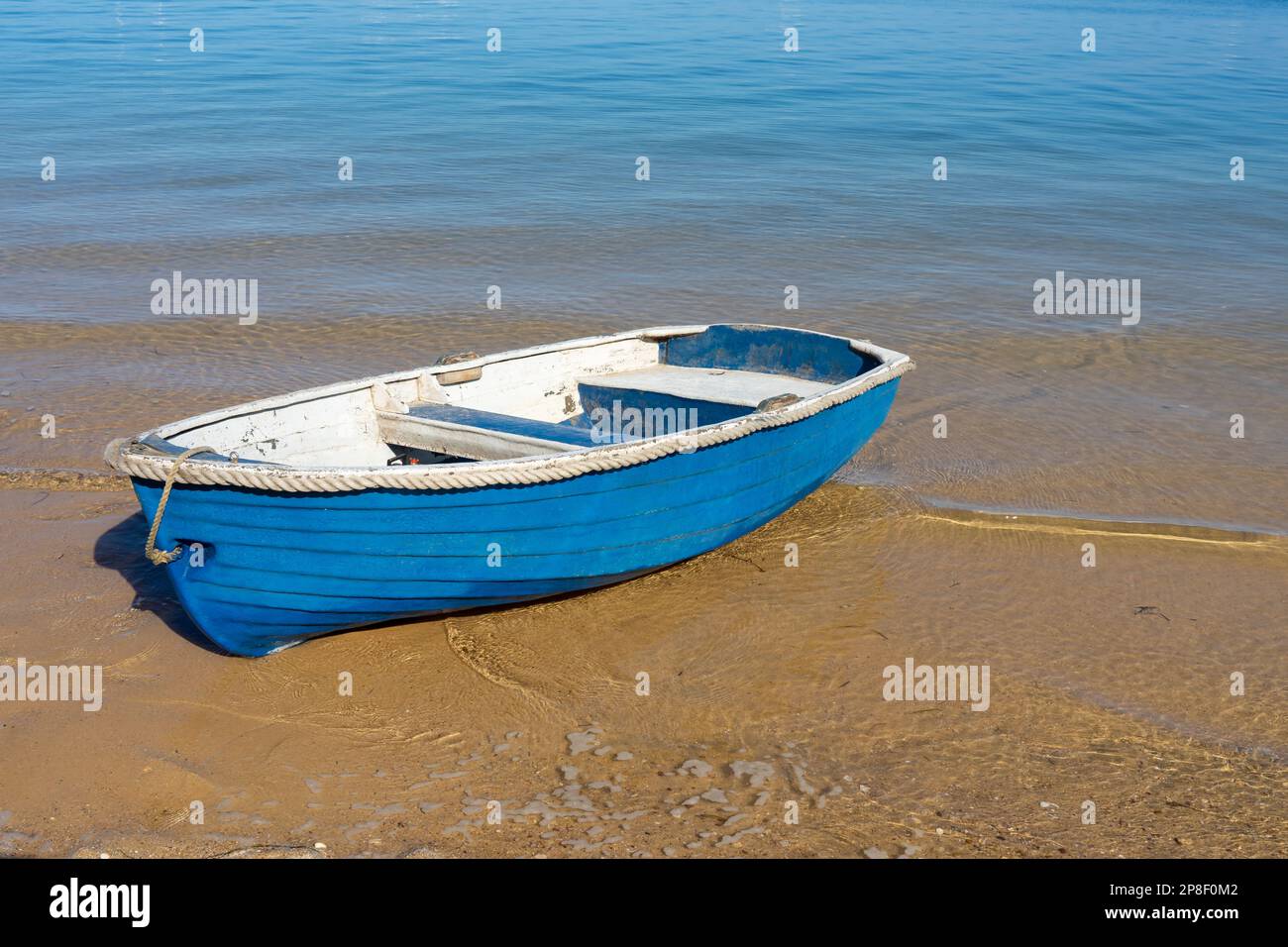 Gentle waves lap a blue rowboat on the resting on the sandy shore. Main ...