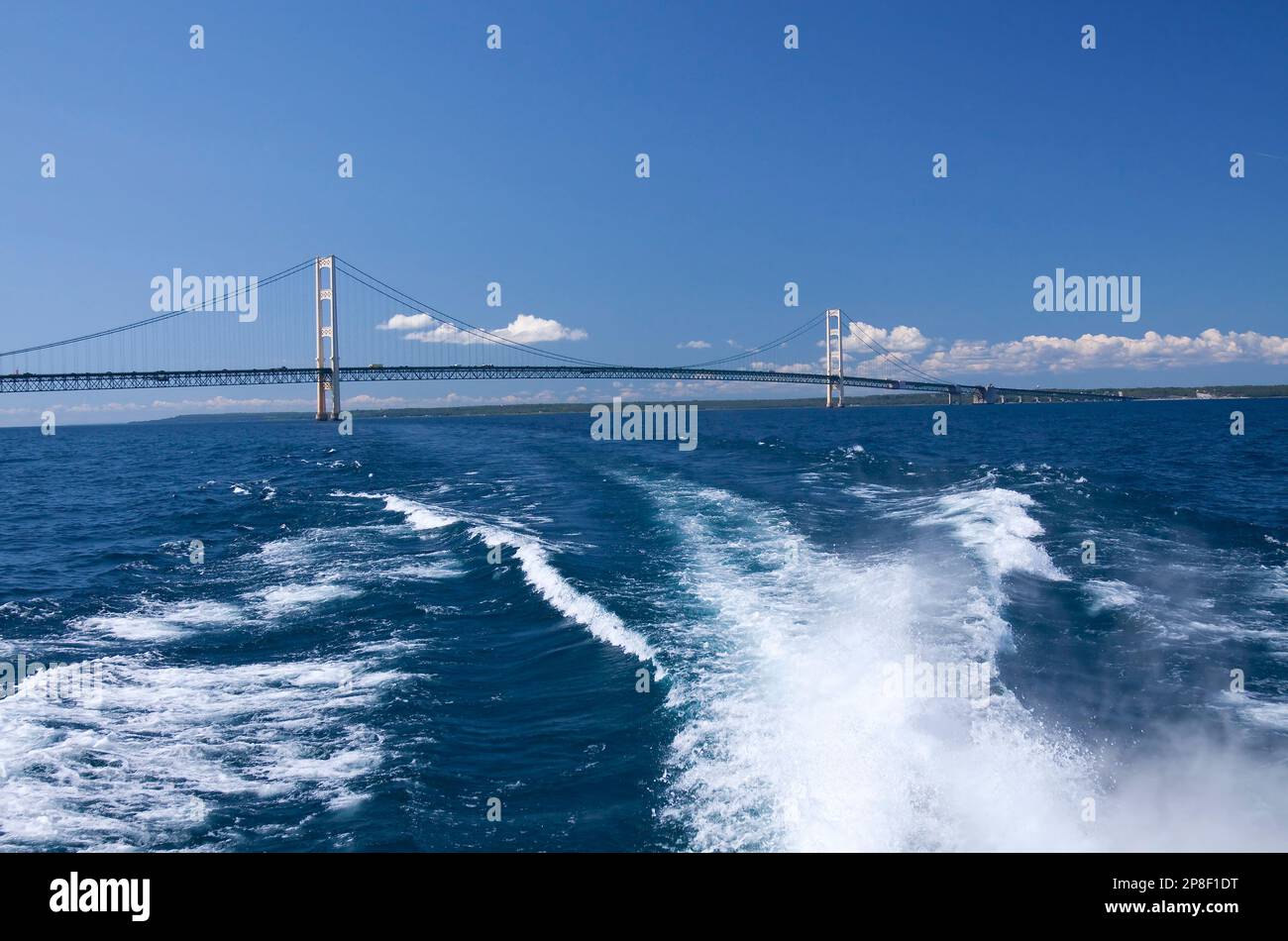 A long suspension bridge with a wake from a boat in the foreground ...