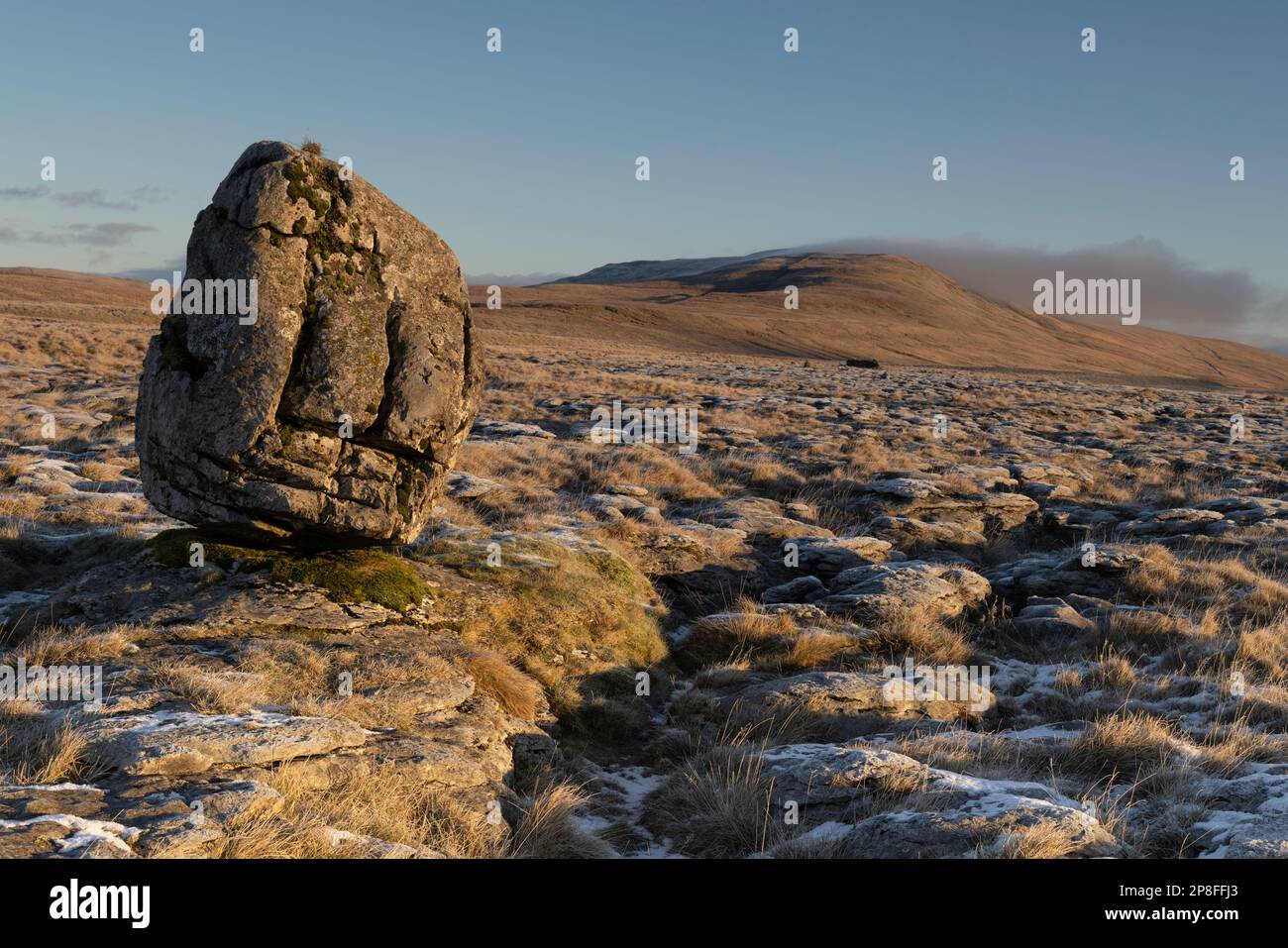A large boulder stands on limestone pavement, with a view of Whernside ...