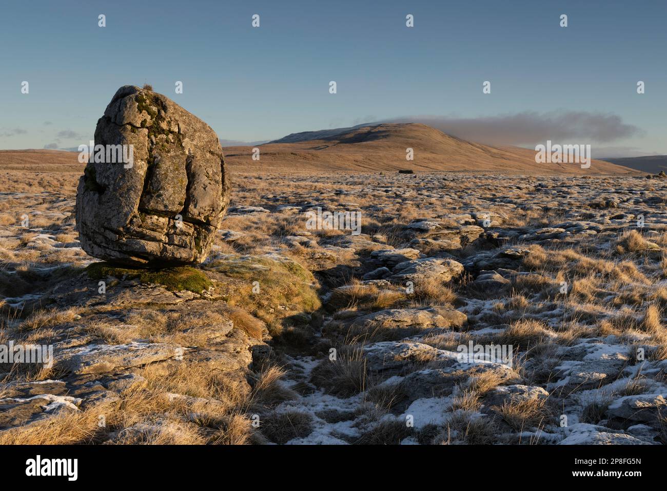 A large boulder stands on limestone pavement, with a view of Whernside ...