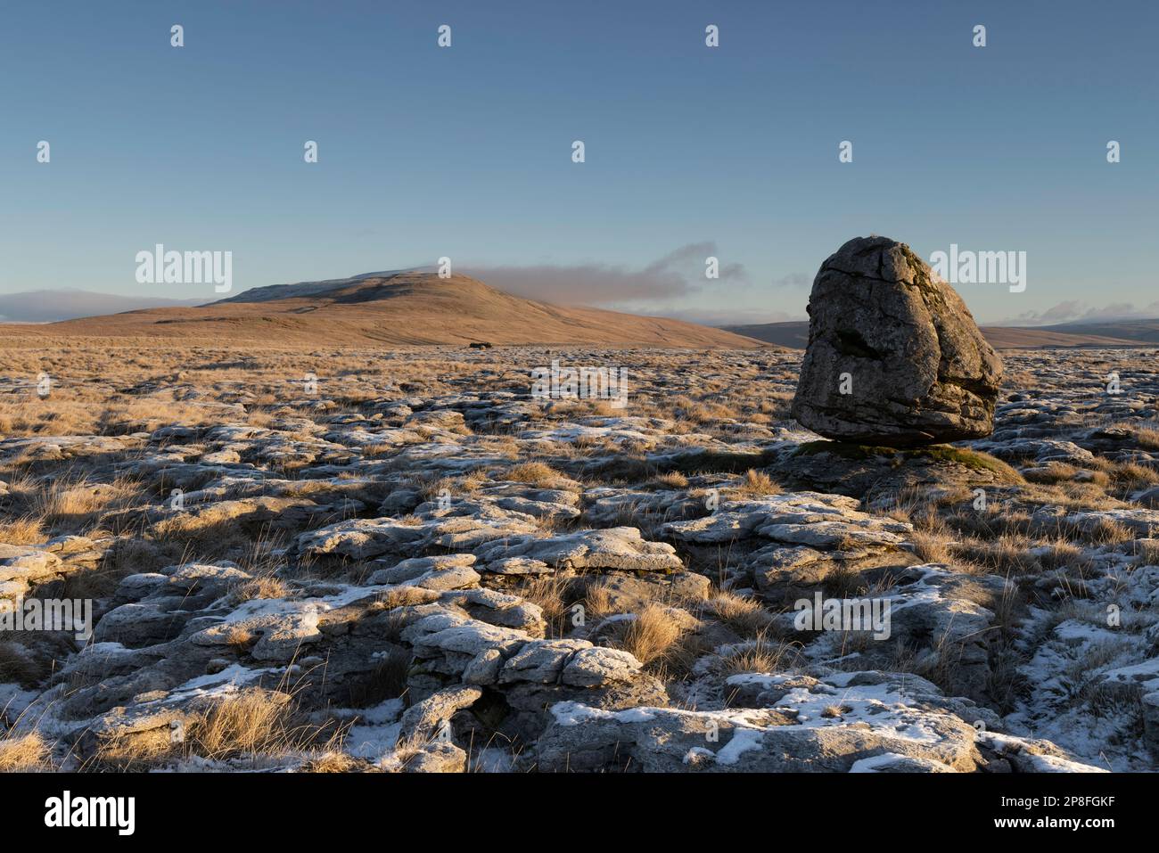 A large boulder stands on limestone pavement, with a view of Whernside ...