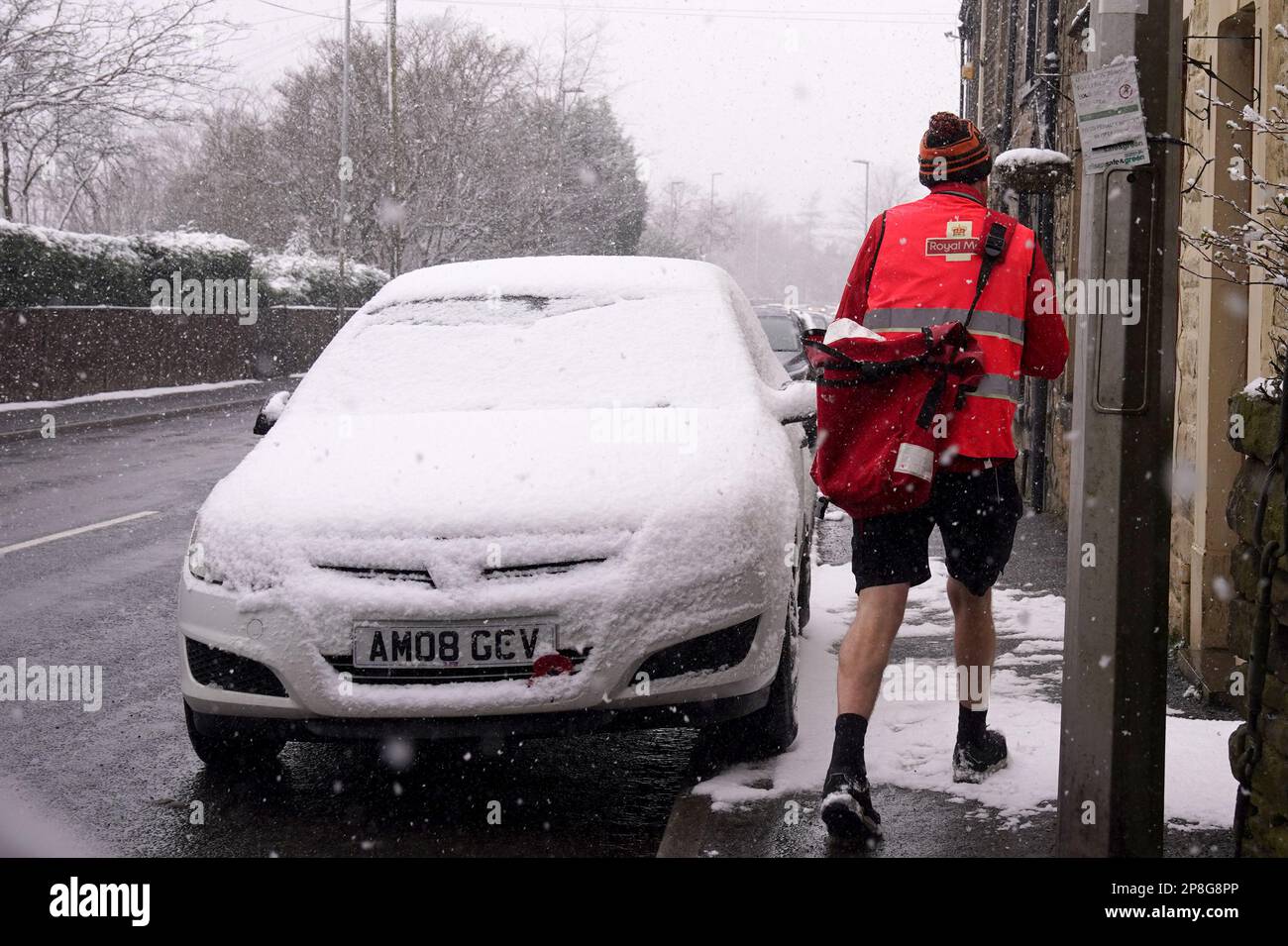 A postal delivery worker wearing shorts in heavy snow fall during his ...