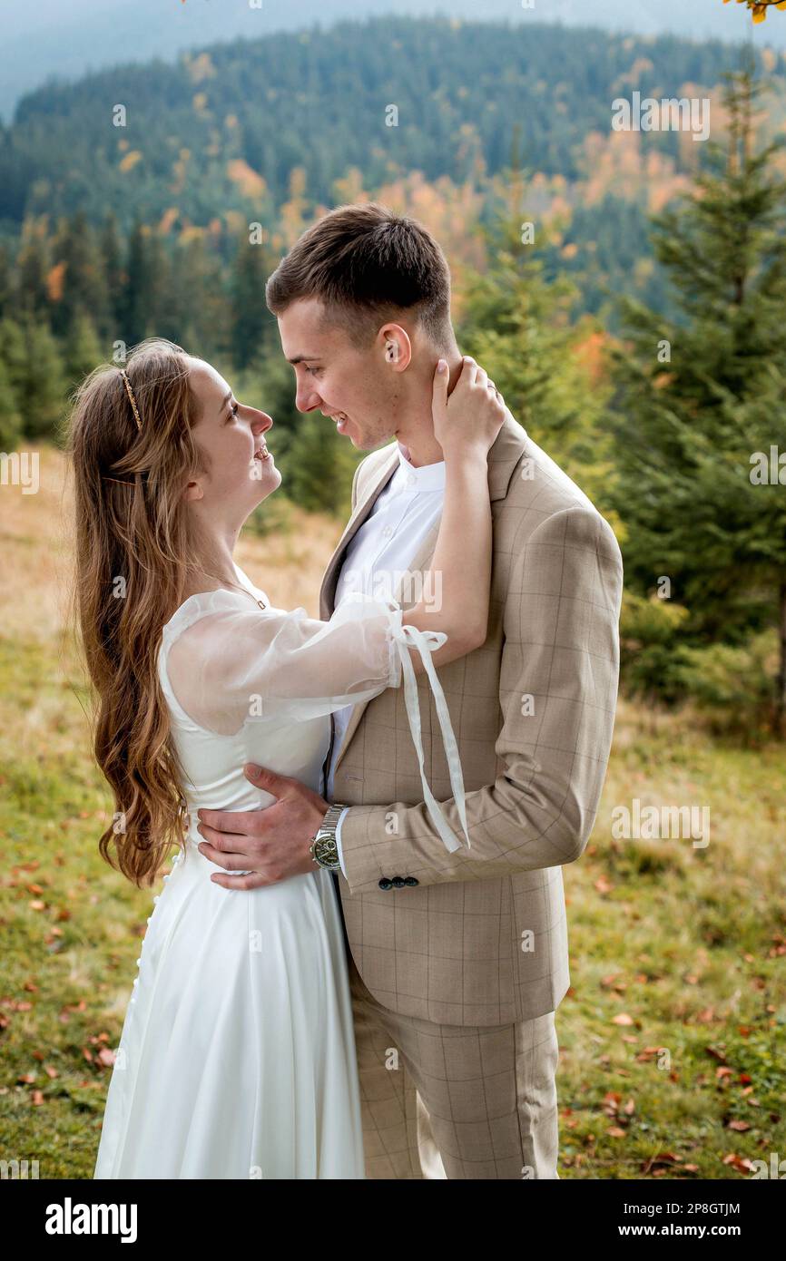 The bride looks at the groom with loving eyes. Smiling newlyweds look ...