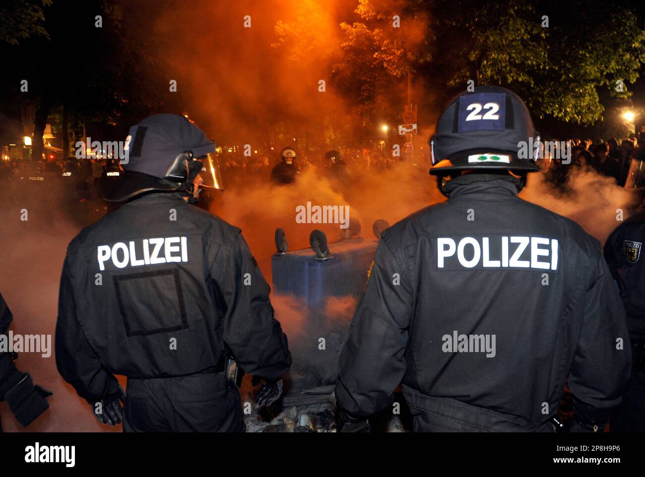 German riot police officers stand next to burning dustbins on a street ...