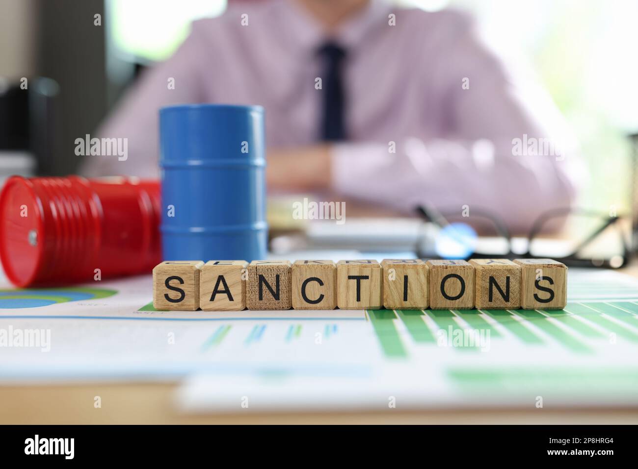 Wooden cubes with word sanction, oil drums and documents on table and ...