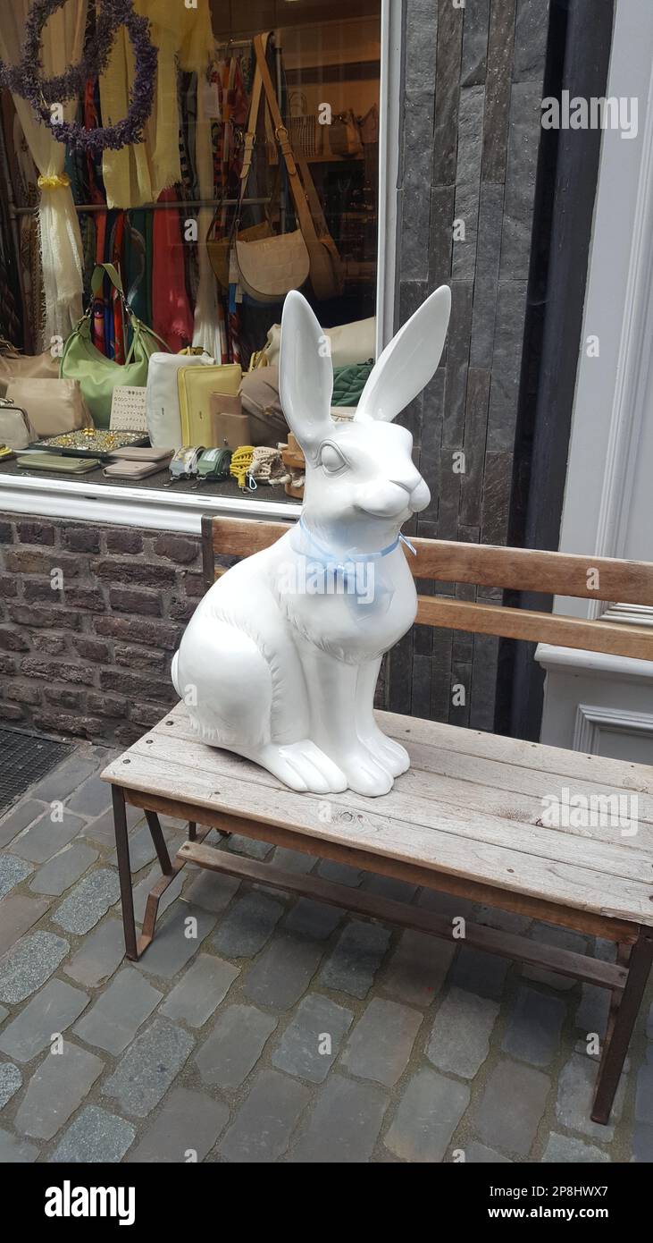 An ornamental white rabbit figurine on a wooden bench in front of a ...