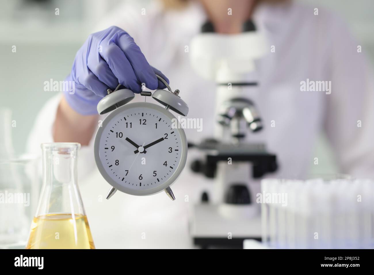 Scientist with test tubes, flask and microscope holds alarm clock in ...