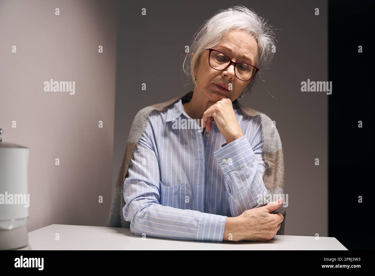 Sad elderly lady sits alone at a table Stock Photo - Alamy