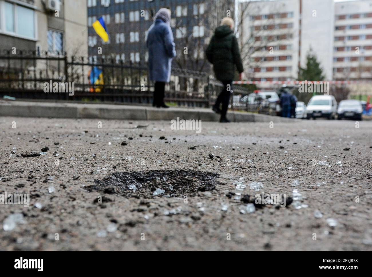 People walk past a small damage on the asphalt and broken glass after ...