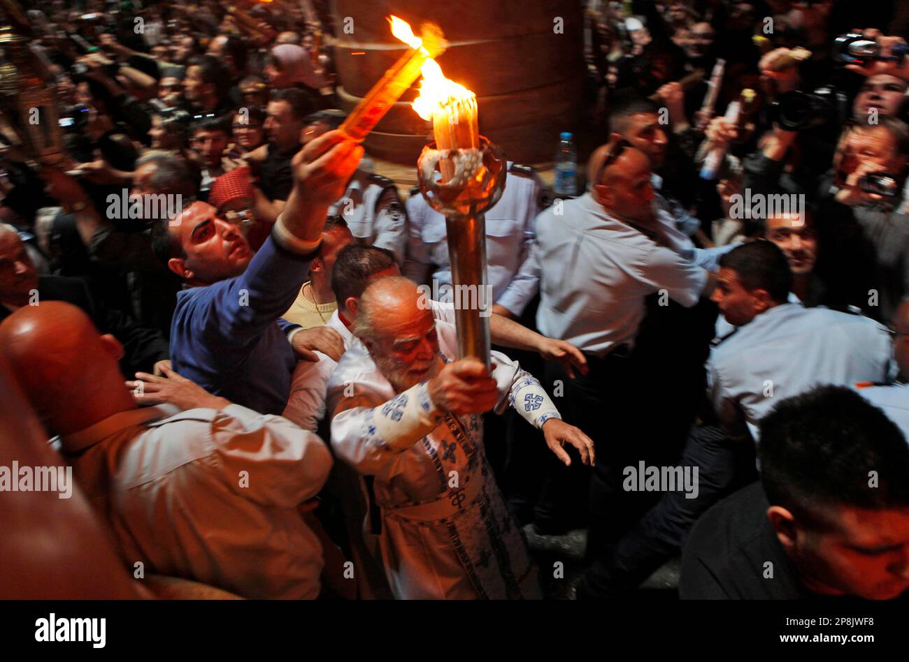 A Greek Orthodox clergyman runs with a torch to light the candles of ...