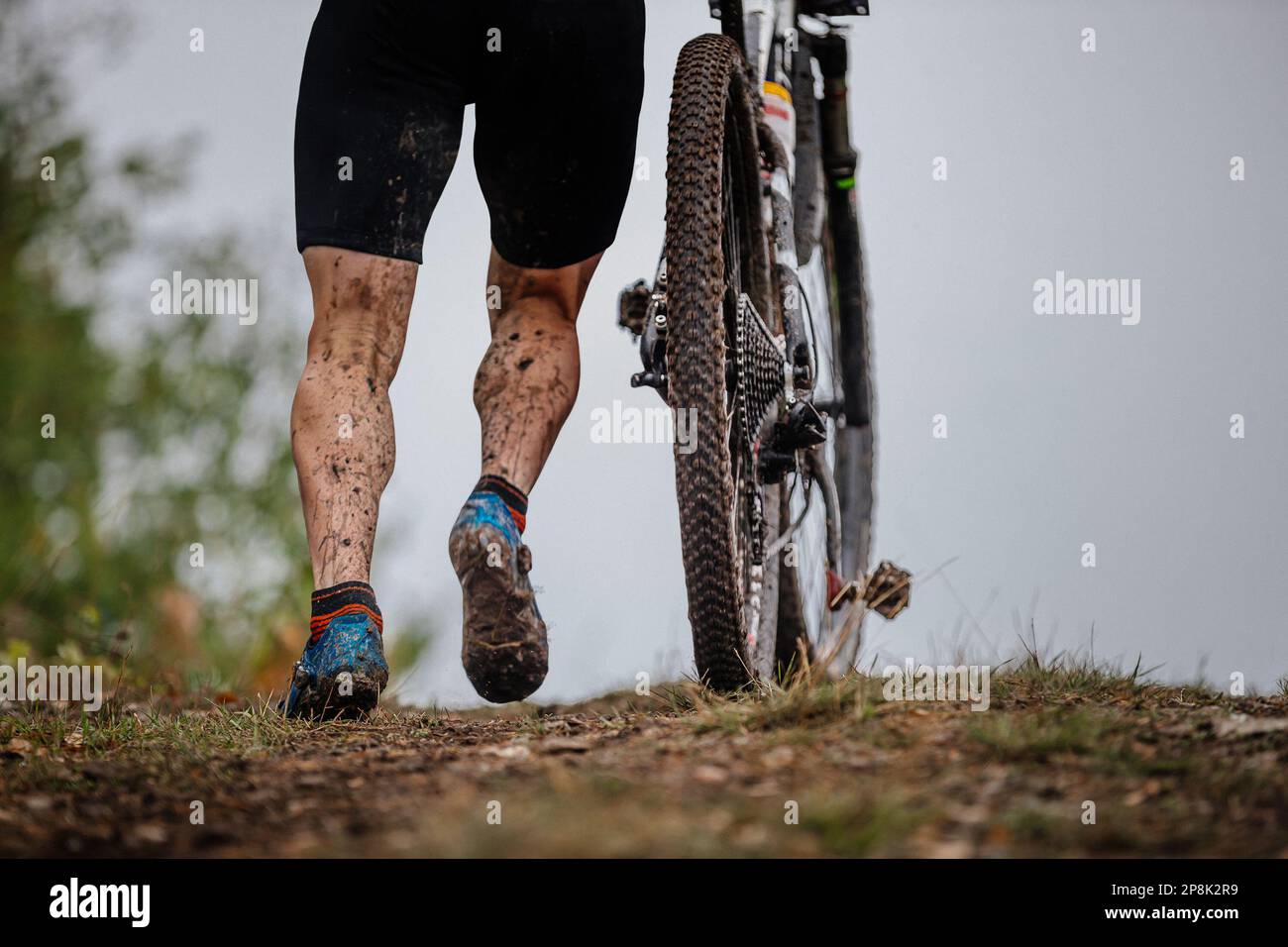 athlete goes uphill with his mountain bike. drops dirt on feet and bike ...