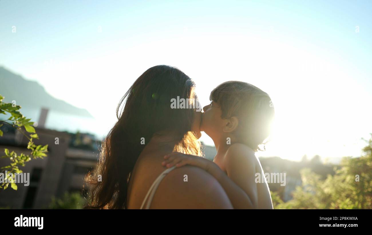 Small boy kissing mother in cheek outside during sunset. Mother holding ...