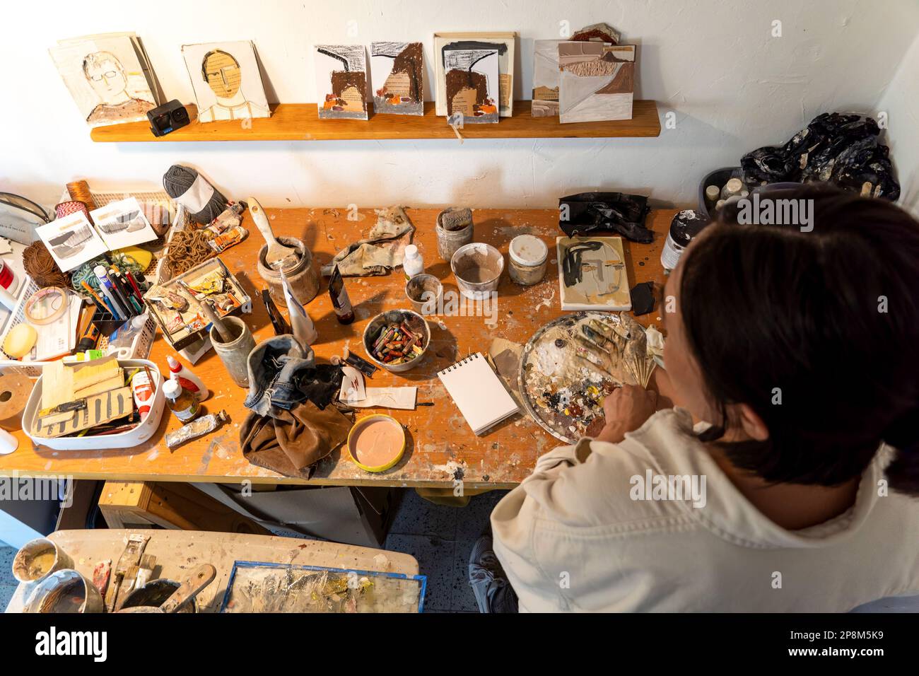 A female artist is sitting at her desk, diligently working on her ...