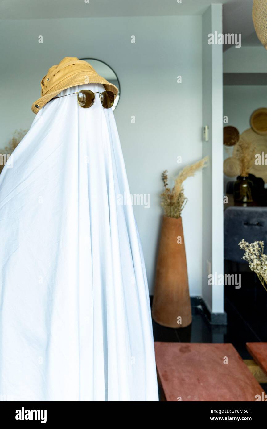 A person wearing a hat and black-rimmed sunglasses over a white cloth ...