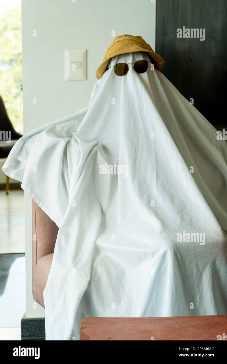 A person wearing a hat and black-rimmed sunglasses over a white cloth ...