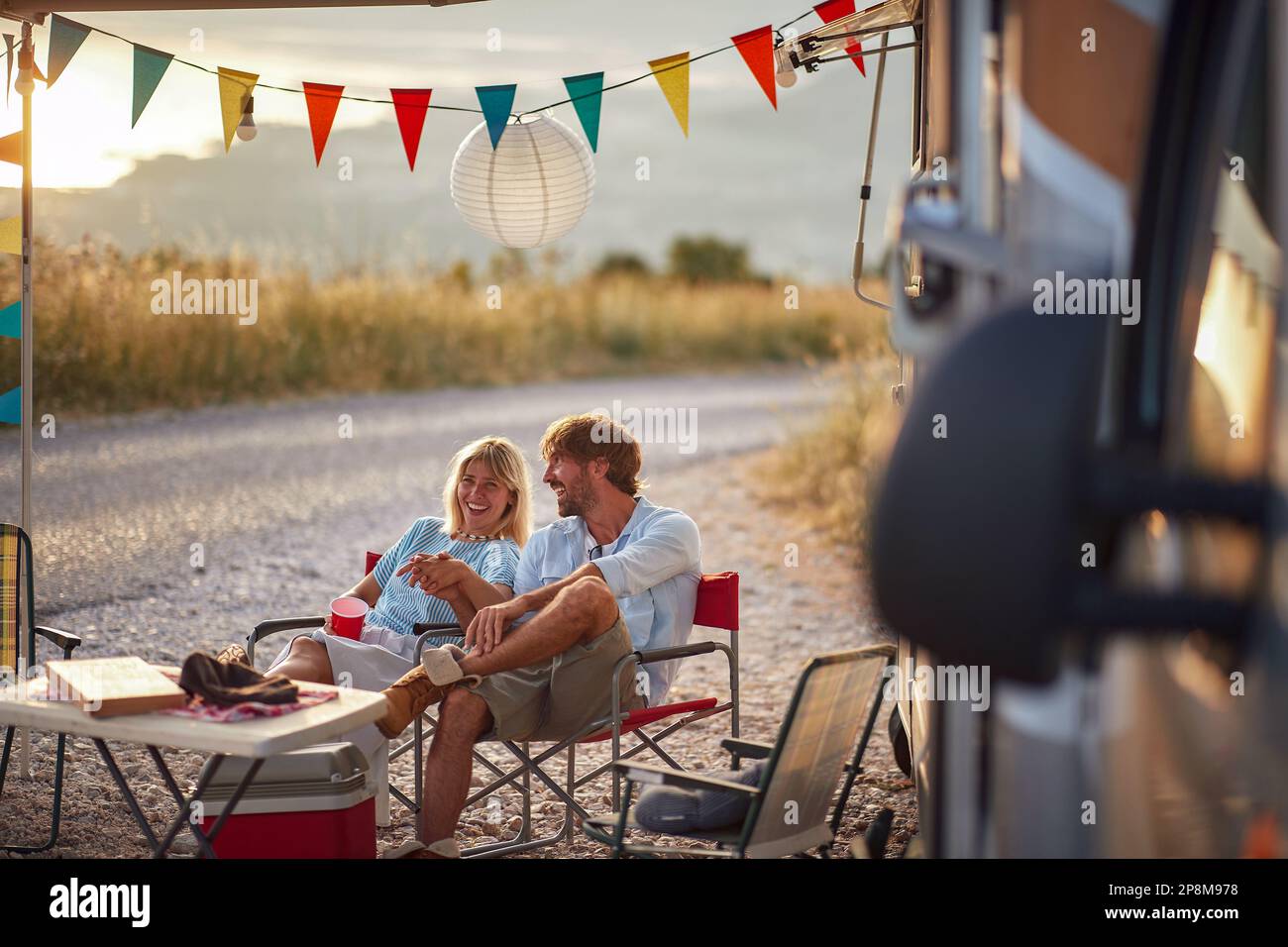 beautiful young adult couple sitting outdoor in front of a camper ...