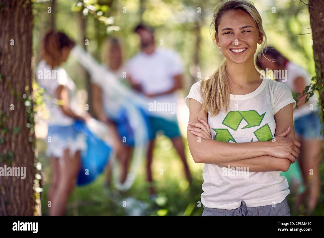 Cheerful young woman volunteer in nature. Group of people cleaning up ...