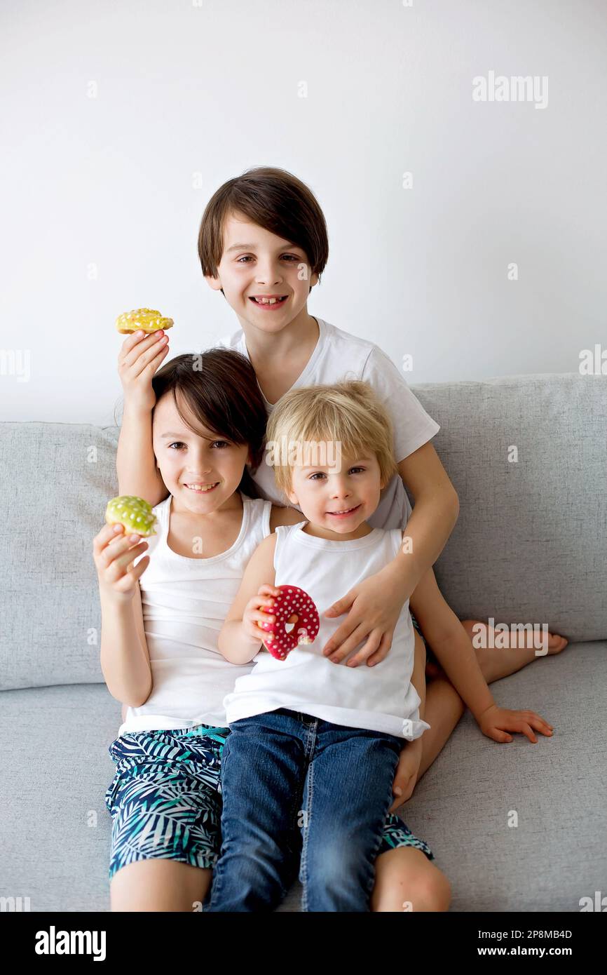 Three children, boy brothers, siblings, eating colorful donuts at home ...