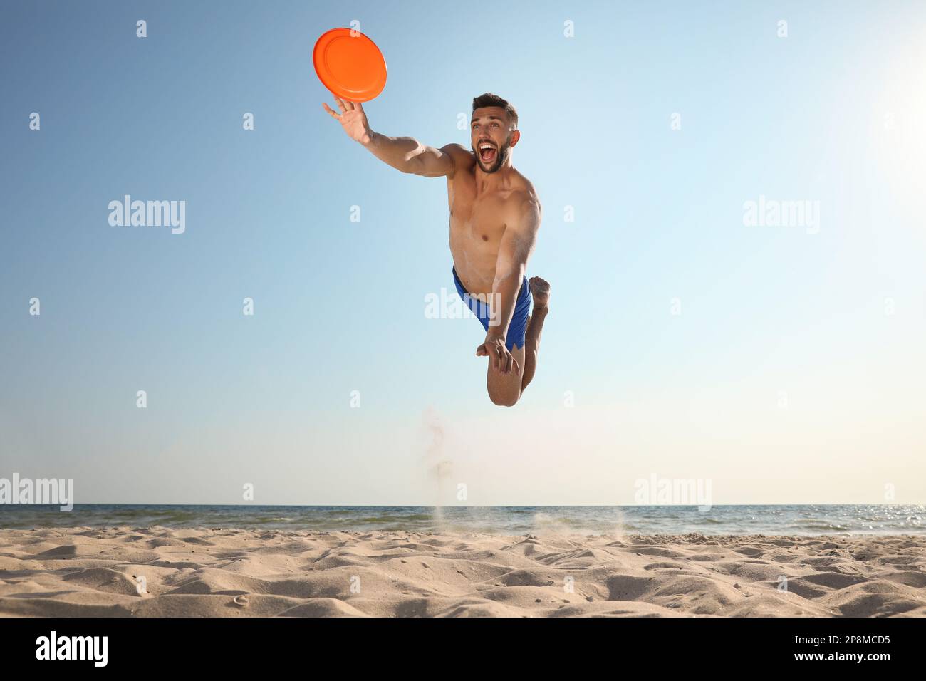 Sportive man jumping while trying to catch flying disk at beach Stock ...