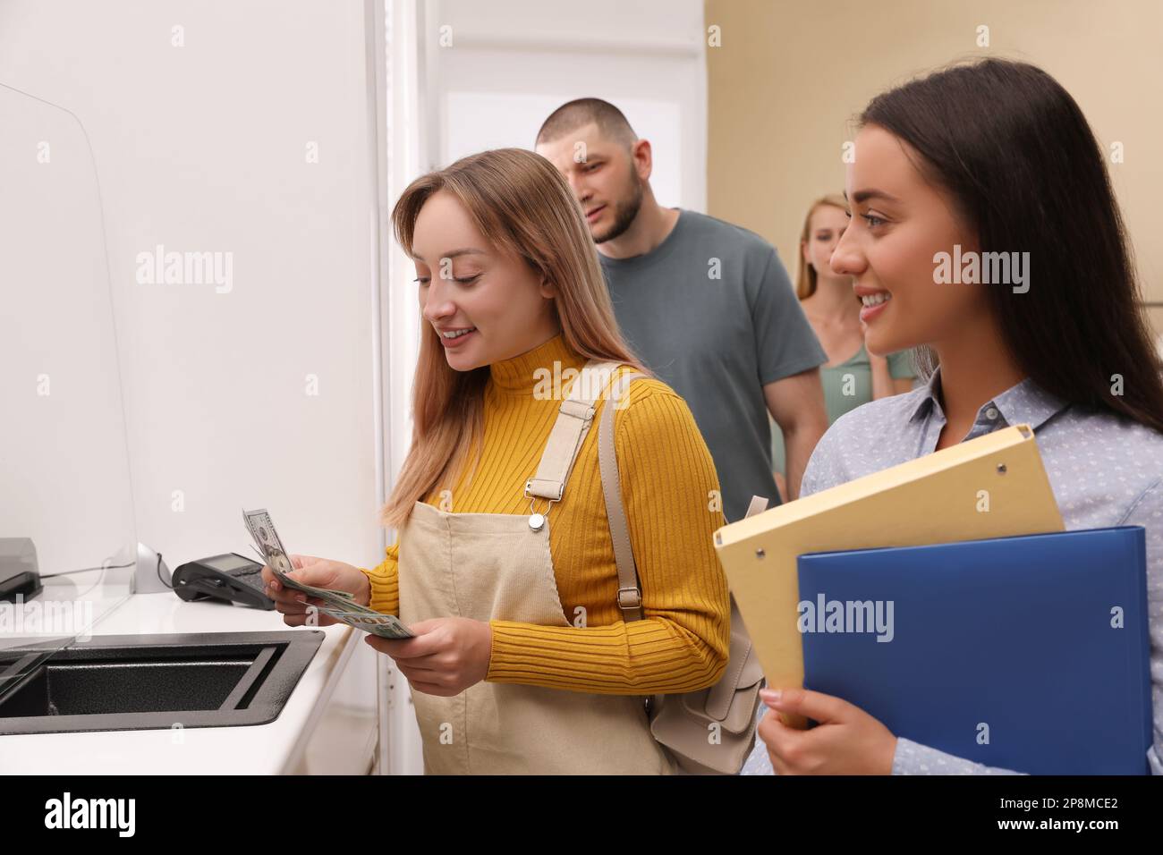 Woman with money and other people in line at cash department window ...