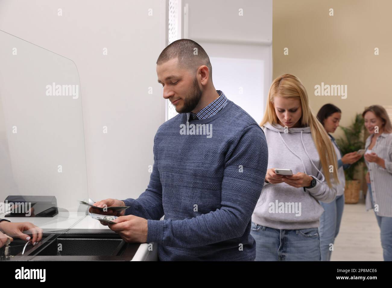 Man with money and other people in line at cash department window ...