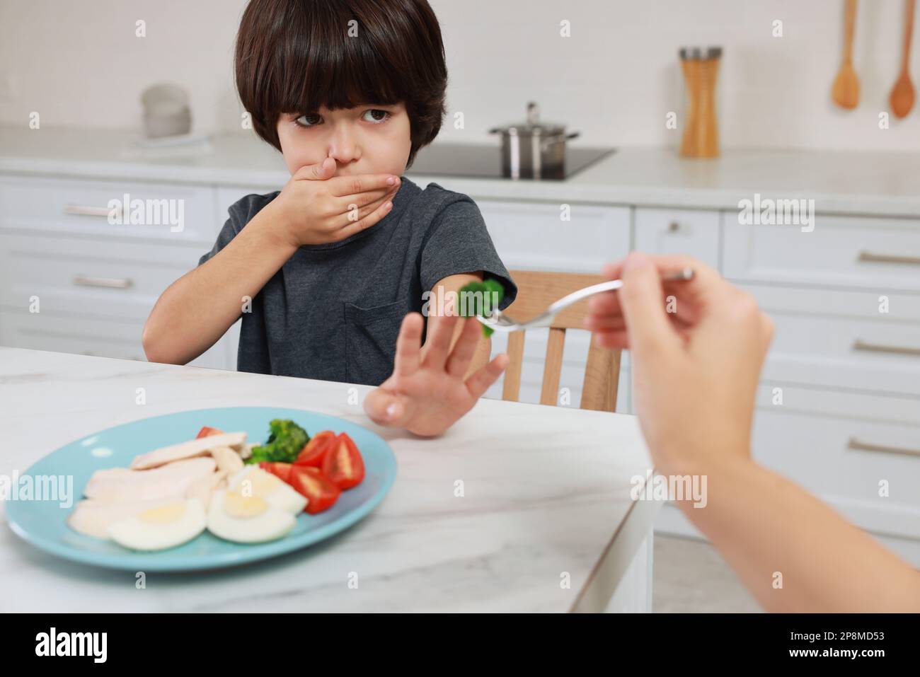 Mother feeding her son in kitchen, closeup. Little boy refusing to eat ...