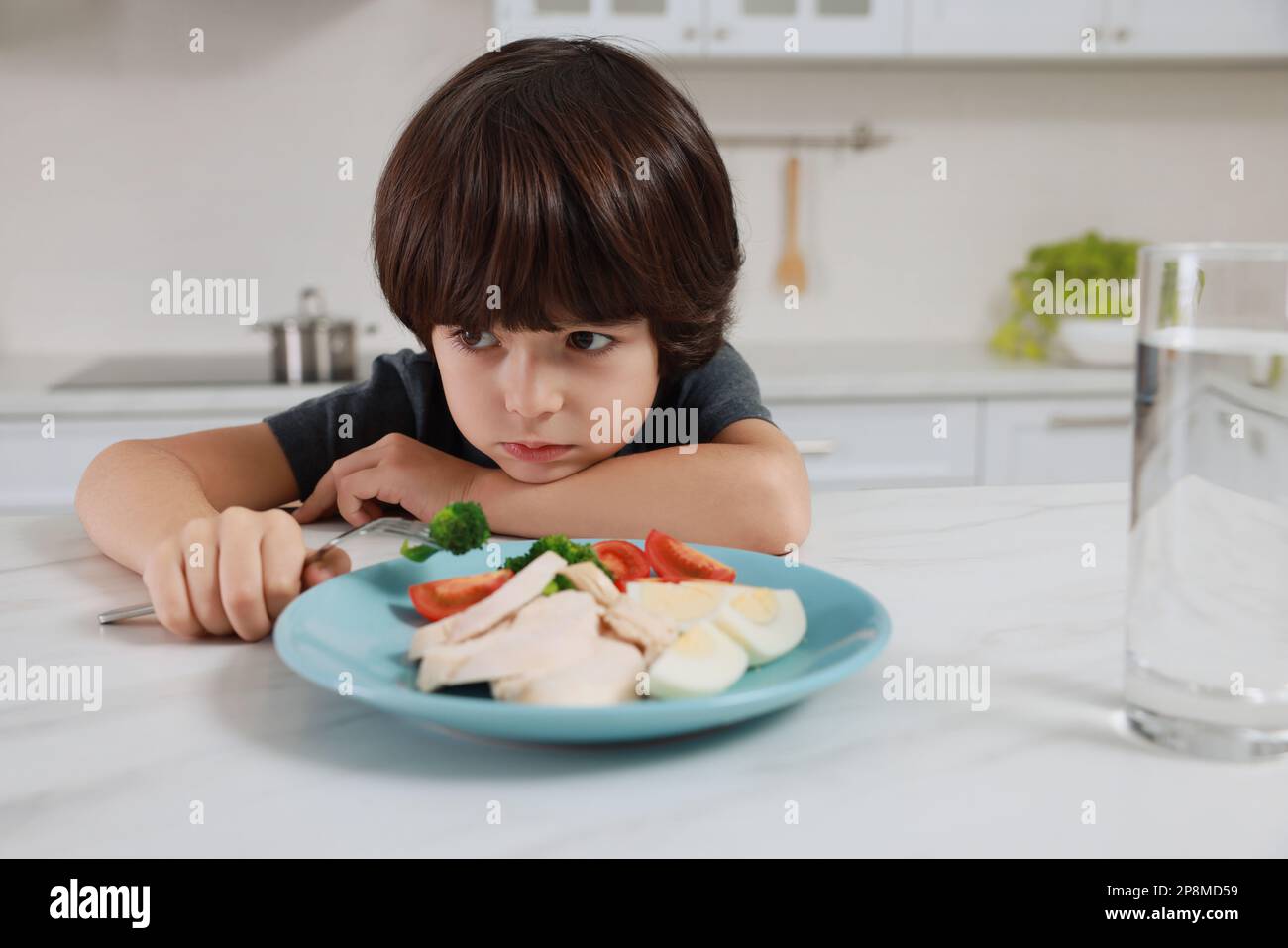 Cute little boy refusing to eat dinner in kitchen Stock Photo - Alamy
