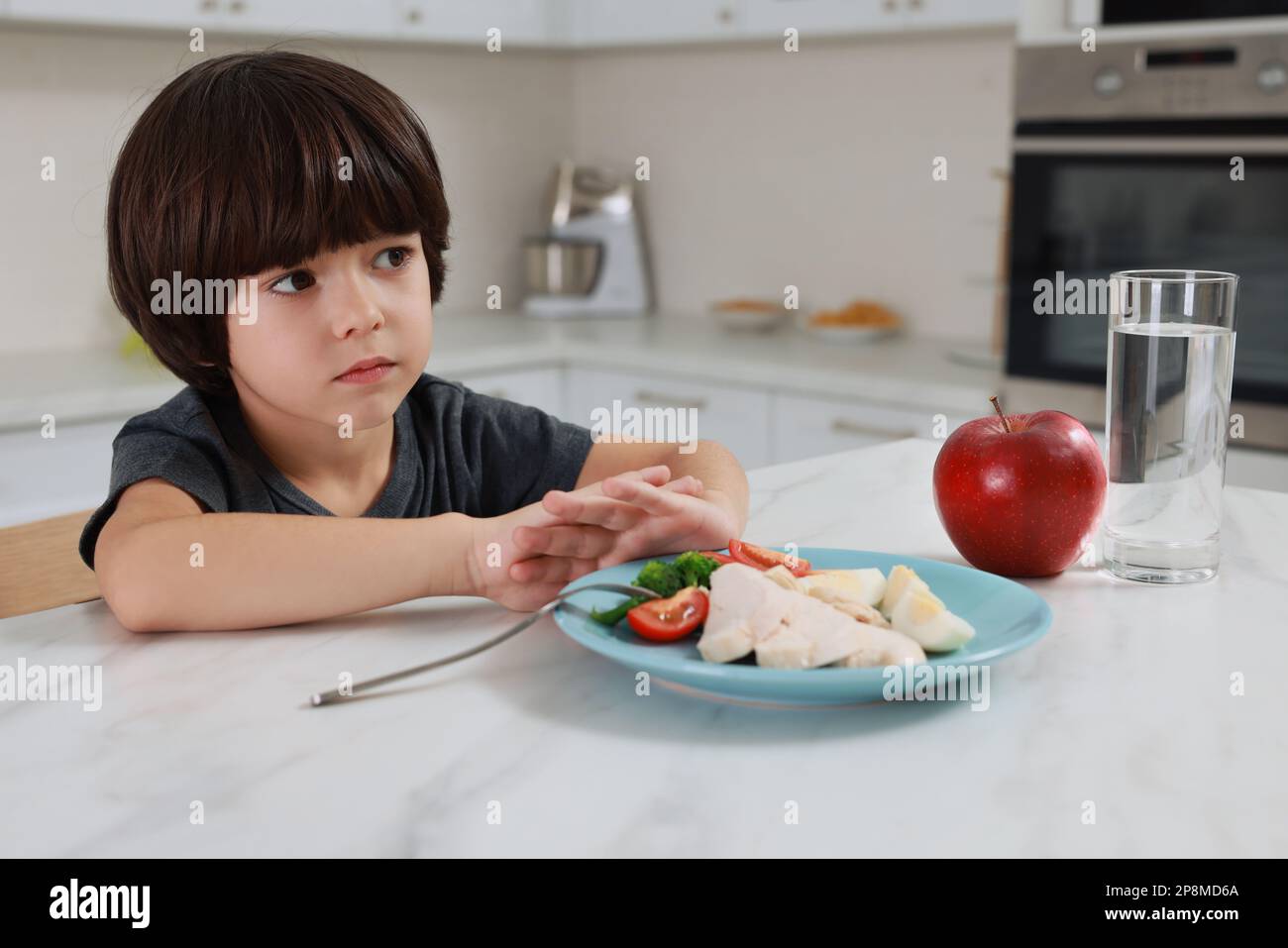 Cute little boy refusing to eat dinner in kitchen Stock Photo - Alamy