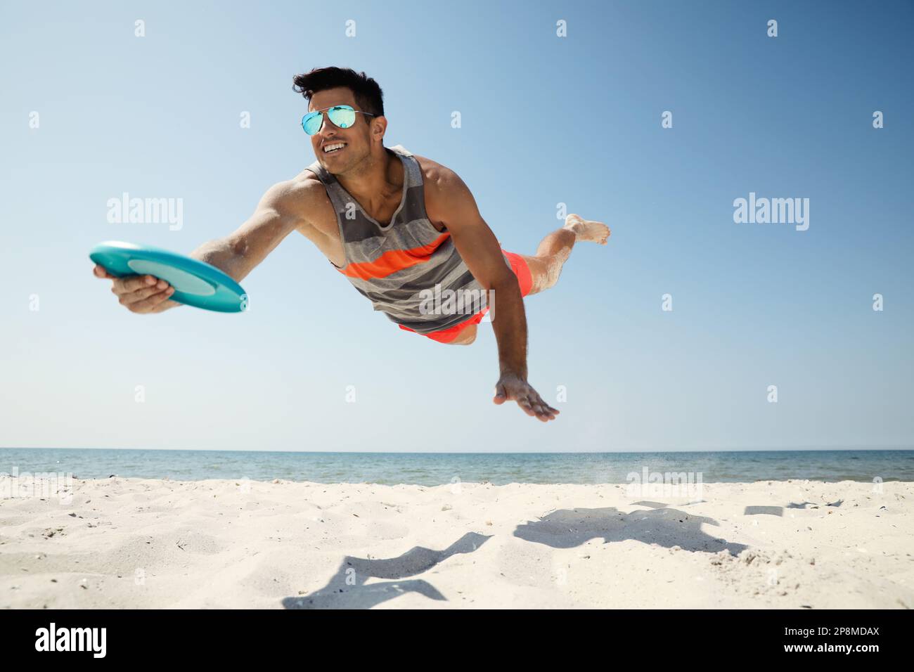 Sportive man jumping and catching flying disk at beach Stock Photo - Alamy